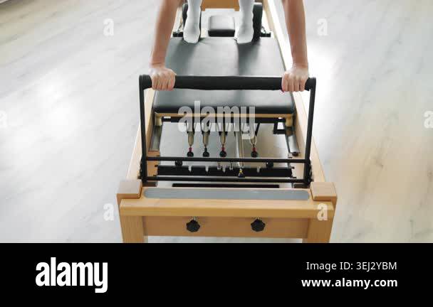 Athletic woman exercising on Pilates reformer machine during strength ...