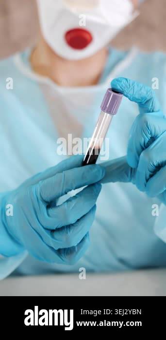 Scientist in protective equipment examining blood sample tube during ...