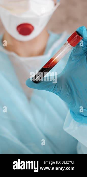 Scientist in protective medical equipment holding blood sample tube for ...