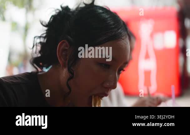 Close up of a young thai woman eating noodles with chopsticks at a ...
