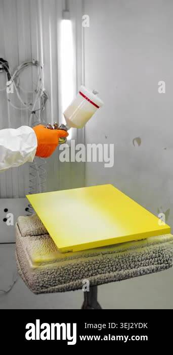 Worker applying yellow paint with spray gun on panel in factory ...