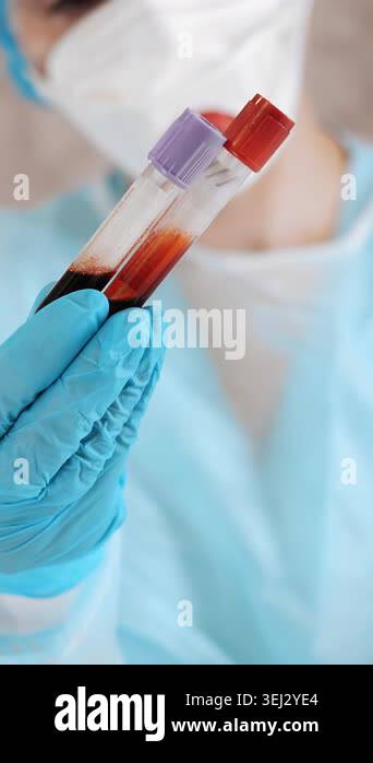 Medical professional in protective equipment holding blood sample tubes ...
