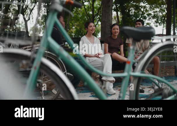 Happy teenagers talking and relaxing on a bench in a park, viewed from ...