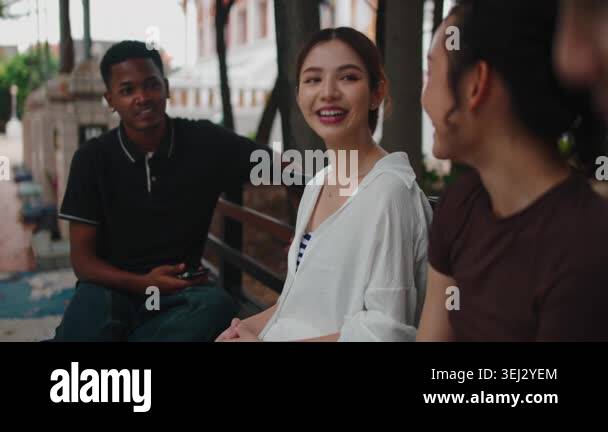 Young diverse friends sitting on a bench, happily talking and laughing ...