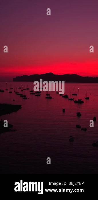 Magnificent red sunset glowing over a calm sea bay with boats anchored ...