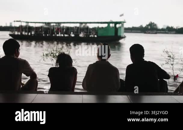 Silhouettes of four people sitting on a dock watching a crowded ...
