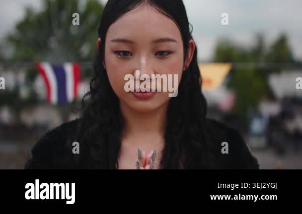 Young asian woman with long nails praying outdoors in thailand with a ...