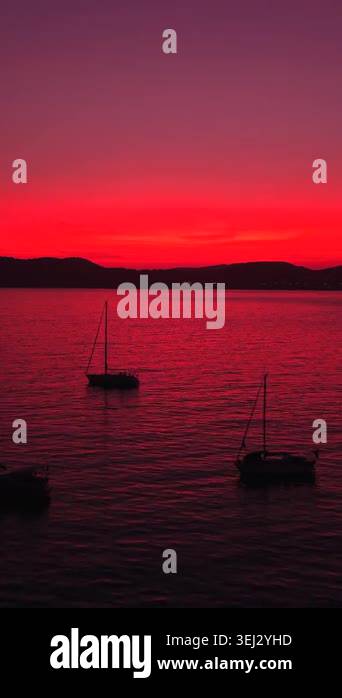 Intense red sunset over the calm sea with silhouetted sailboats ...