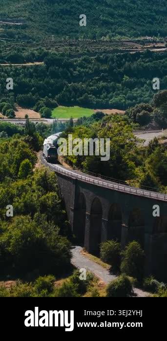 Passenger train traveling on a stone bridge across a beautiful mountain ...