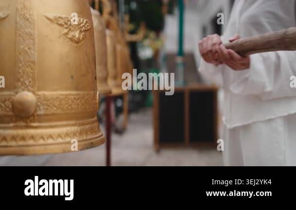 Young woman ringing a row of golden bells with a wooden mallet at a ...