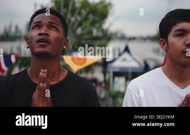 Two young diverse men praying together during a religious ceremony at a ...