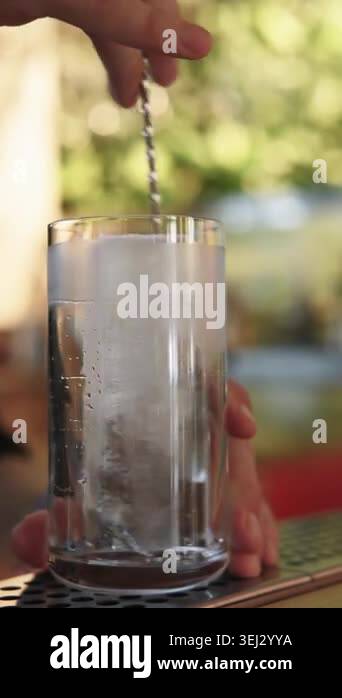Vertical video. Stirring ice. Cocktail making. Barkeeper hand rotating ...