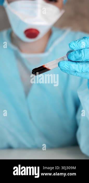 Scientist in protective medical equipment holding blood sample tube ...