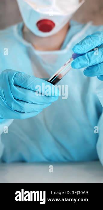 Scientist in protective equipment handling blood sample tube during ...