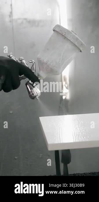 Close up of worker using spray gun to paint wooden panel in industrial ...