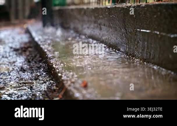 Close up macro view of heavy rain drops splashing on wet concrete curb ...