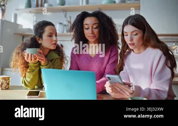Multi-ethnic friends browsing laptop standing together home kitchen ...