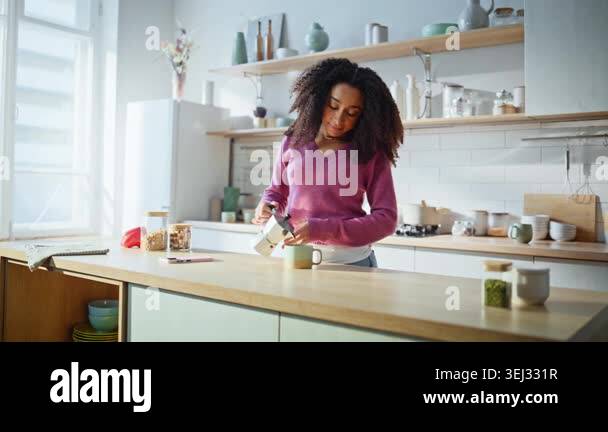 Woman pouring fresh coffee from coffeemaker at wooden kitchen counter ...