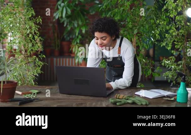 African woman florist gardener working in botanical store using laptop ...