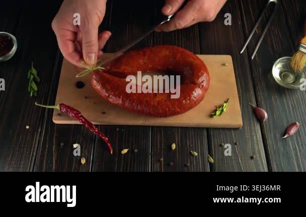 The hands of a chef cutting a sausage string on a wooden cutting board ...