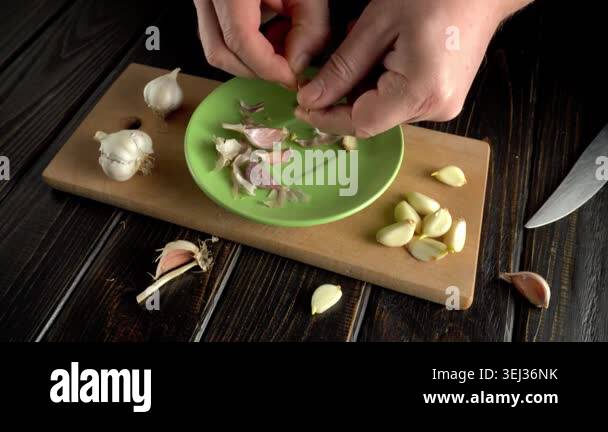 Hands carefully peel garlic cloves from a bulb, placing them on a green ...