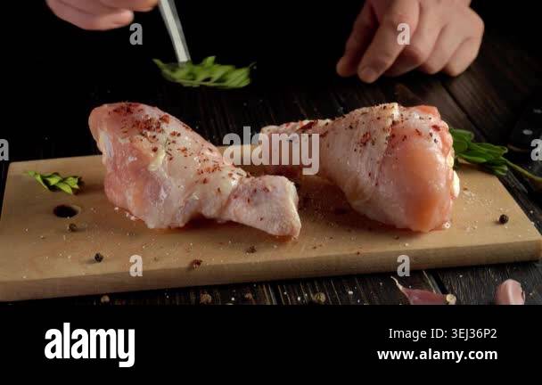 Chef prepares raw chicken drumsticks by adding herbs and spices on a ...