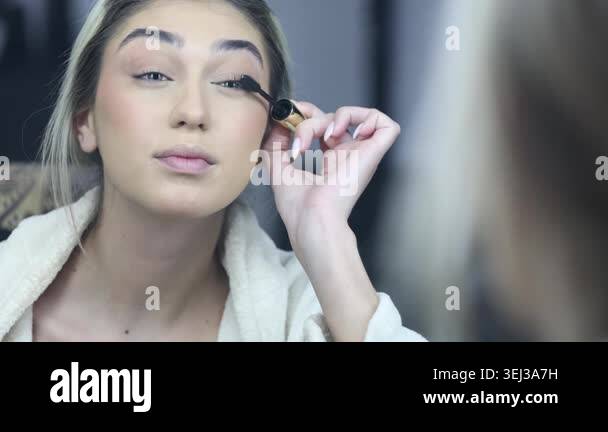 4K slow motion video of young woman applying mascara to eyelashes while ...