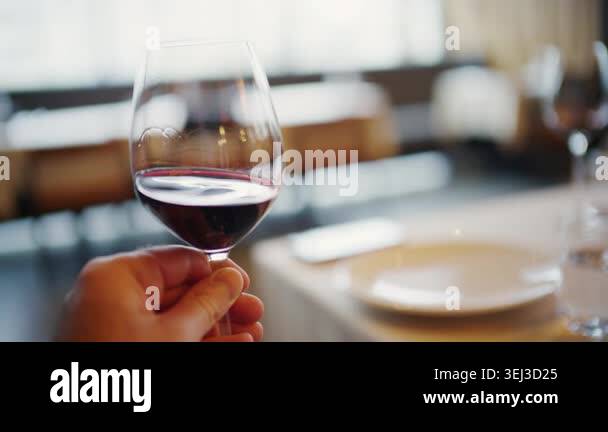 Close up of a hand holding a glass of red wine in a softly lit ...