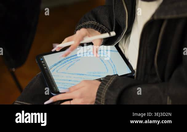 Close up of a person drawing on a tablet with a white stylus, creating ...