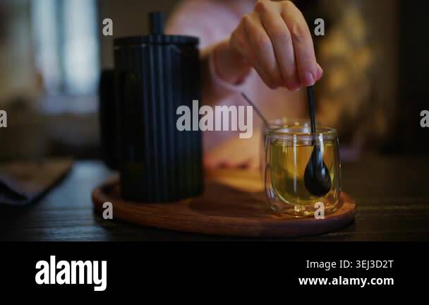 Close up of a woman preparing tea, gently stirring a warm drink in a ...