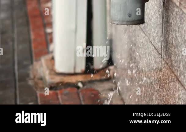 a metal drain pipe pouring out water against a concrete wall Stock ...