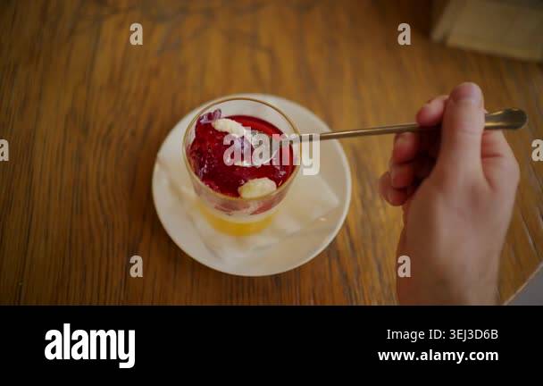 Close up of a spoon lifting a piece of bright red fruit jelly from a ...