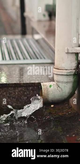 a metal drain pipe pouring out water against a concrete wall Stock ...