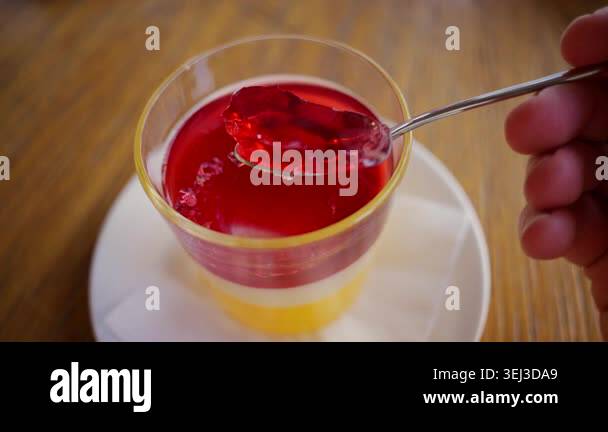 Close up of a spoon lifting a piece of bright red fruit jelly from a ...
