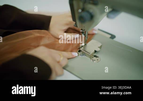Close up of a person guiding brown sheer fabric under the needle of an ...