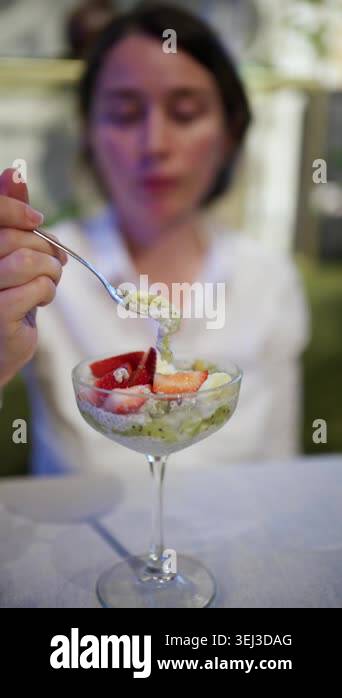 A woman holds a spoonful of chia pudding in front of a dessert glass ...