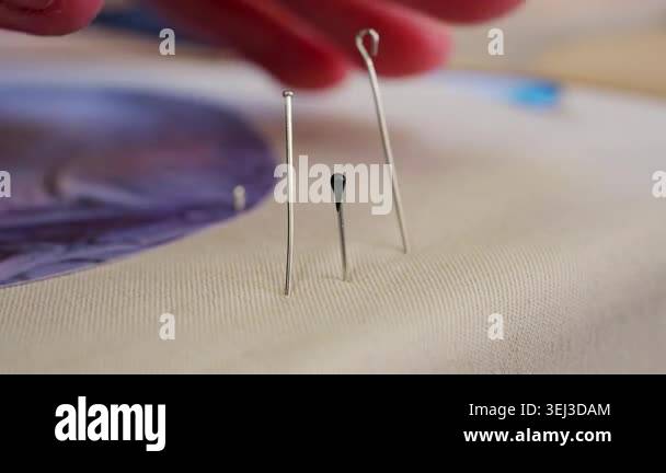 Macro shot of two thin metal sewing pins standing upright in beige ...