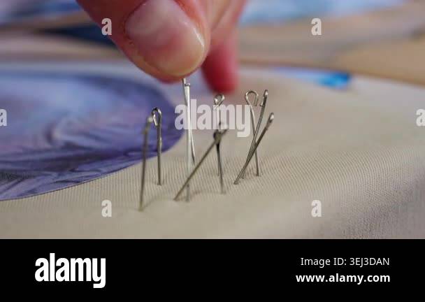 Close up of a hand placing several metal sewing pins into beige fabric ...