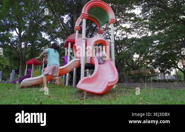 Cute young Asian girl having fun sliding down a purple slide at the ...