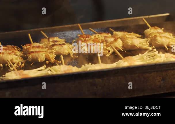 Close-up of bacon wrapped enoki mushroom skewers cooking on a flat top ...