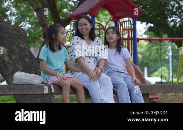 Happy Asian mother and her two young daughters sitting on a bench and ...