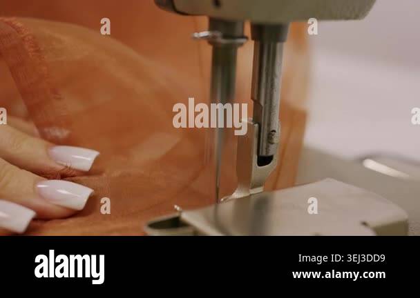 Close up of a person guiding brown sheer fabric under the needle of an ...