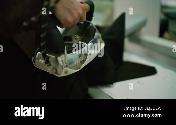 Close up of a tailor using a professional steam iron on black fabric in ...