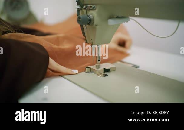 Close up of a person guiding brown sheer fabric under the needle of an ...