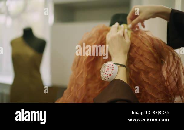 Designer's hands hold a round pin cushion filled with silver dressmaker ...