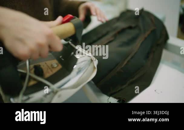 Close up of a tailor using a professional steam iron on black fabric in ...