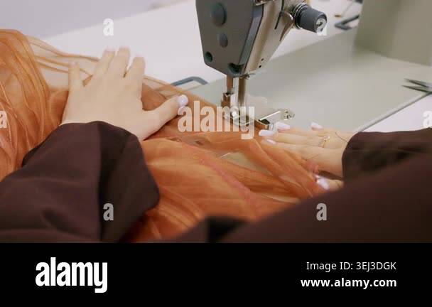 A fashion designer guides translucent orange organza fabric under the ...