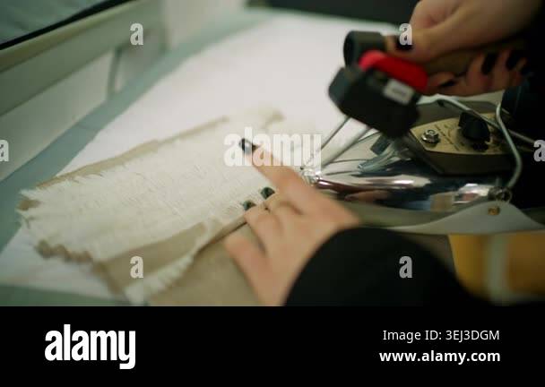 Designer's hands use a professional steam iron to press white fringed ...