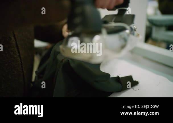 Close up of a tailor using a professional steam iron on black fabric in ...