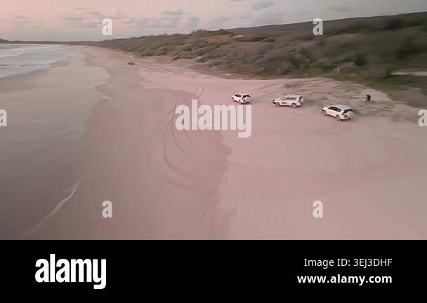 4WD vehicles parked on Fraser Island beach at sunrise drone view. High ...